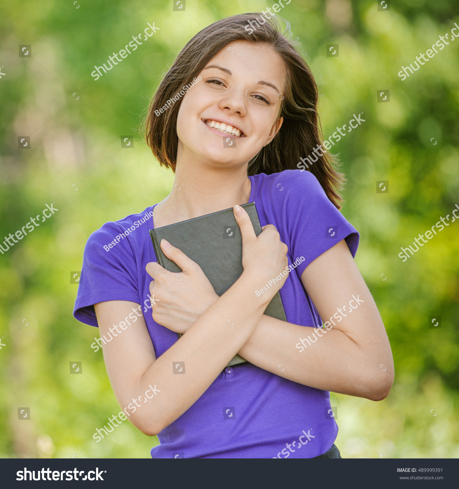 Portrait of young smiling cheerful woman in violet blouse reading interesting book at summer ...