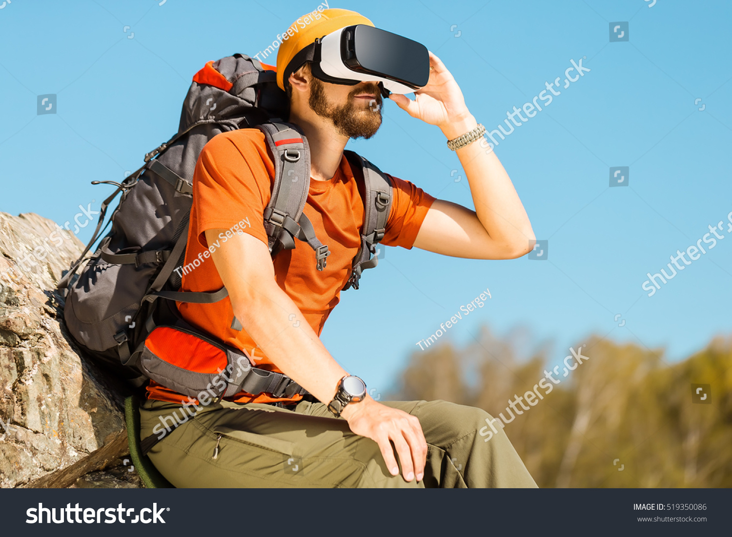 Successful young man using virtual reality goggles to tour in mountains ...
