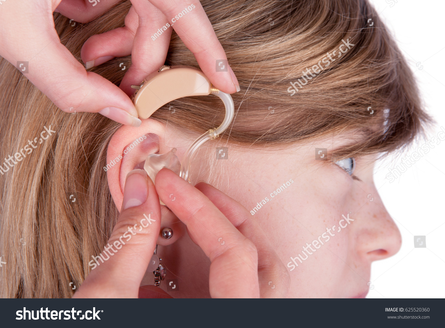 Close up of an ear and hands inserting a hearing aid into ear. Studio ...