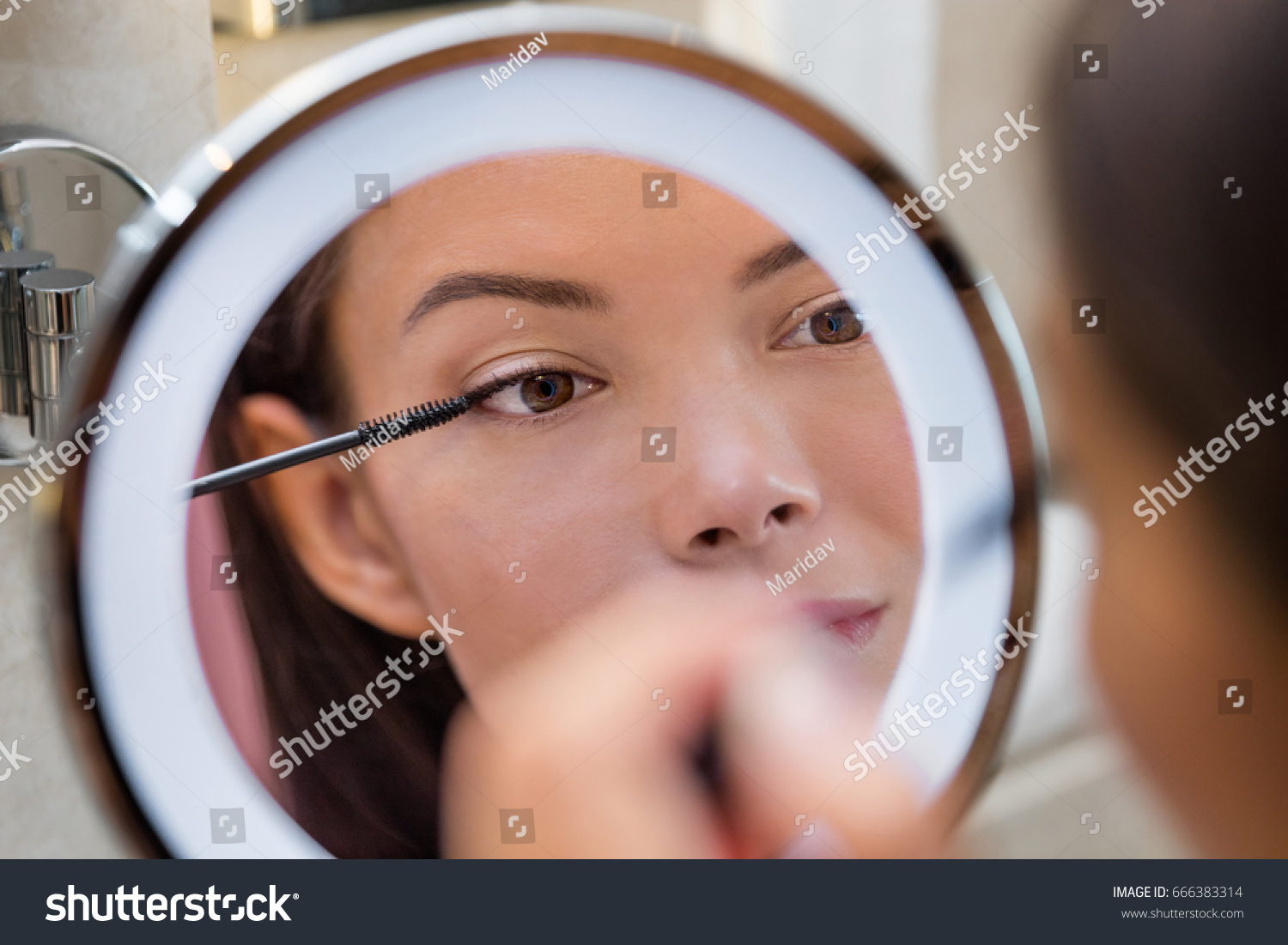 Woman putting mascara in ring light round makeup mirror at home ...