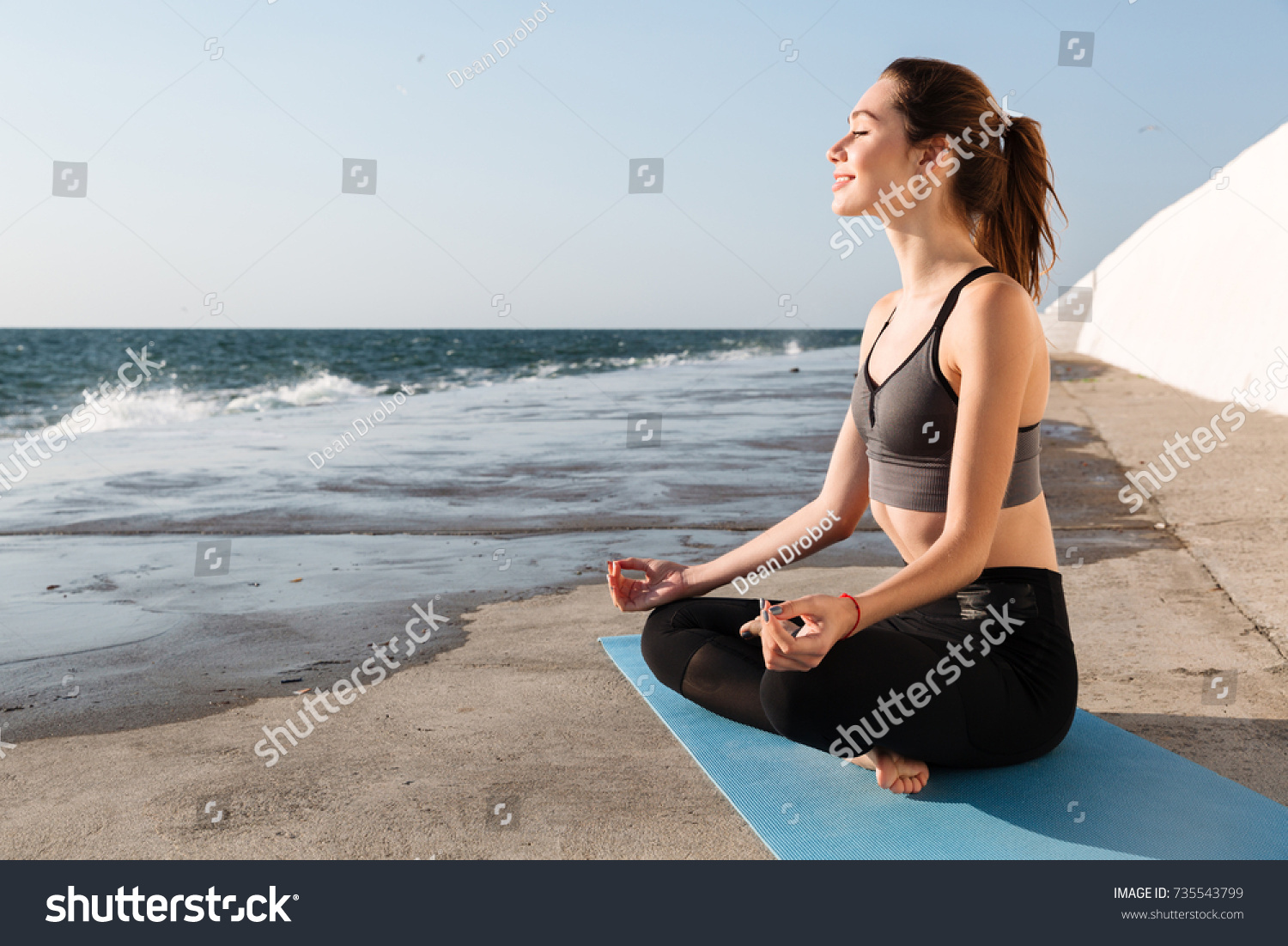 Portrait of cheerful brunette in sportwear sitting in lotos pose while ...