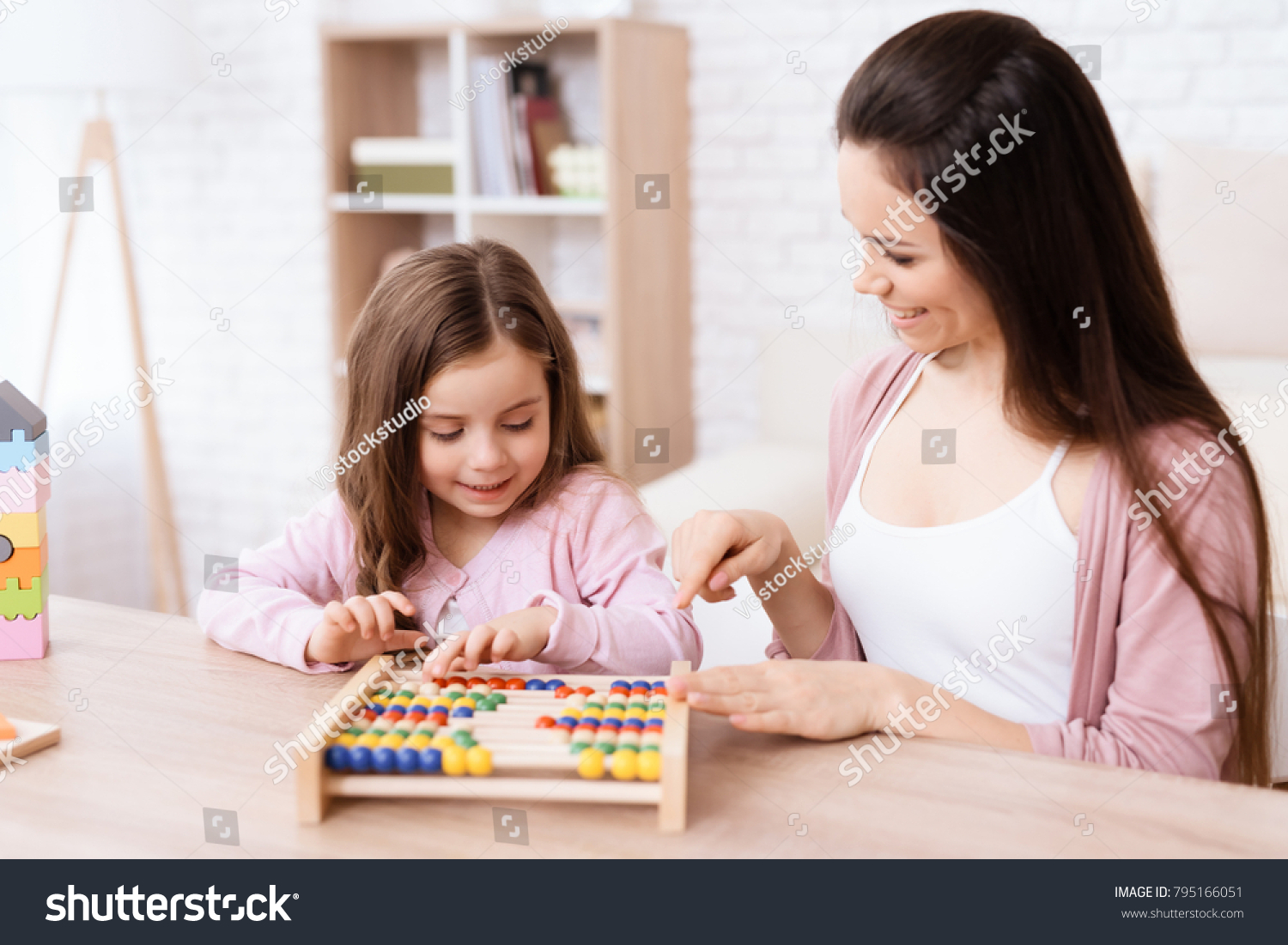 Young woman teaches a little girl math on wooden abacus. The girl is ...